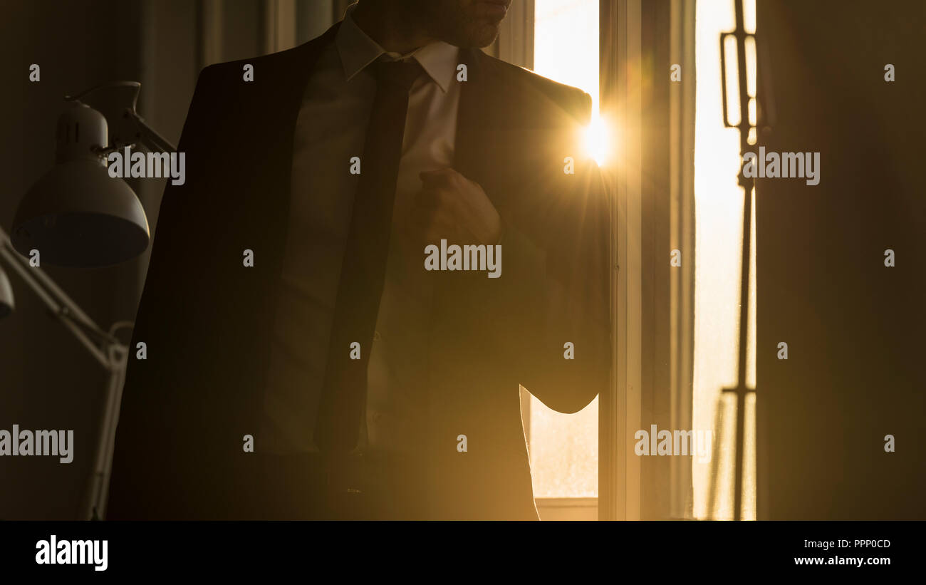Businessman leaning on a window frame in a shadowy office with a bright ...