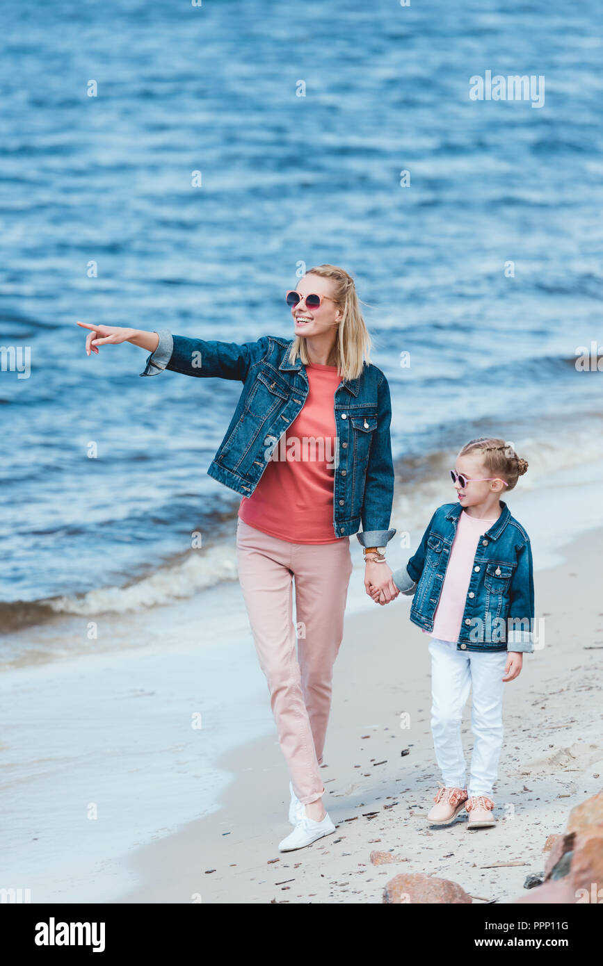 family holding hands and walking on sea shore, mother pointing ...