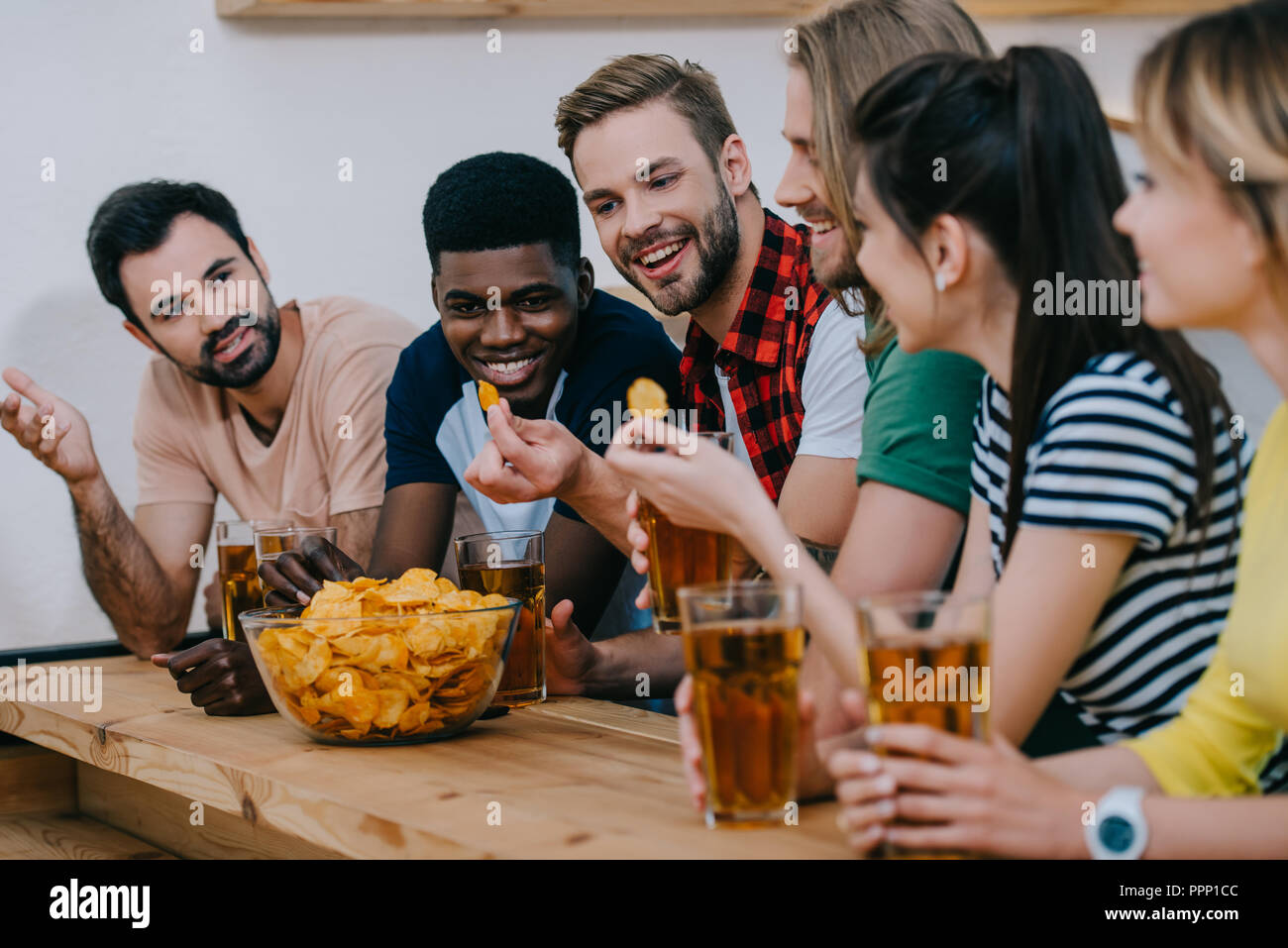 smiling group of multicultural friends eating chips, drinking beer and ...