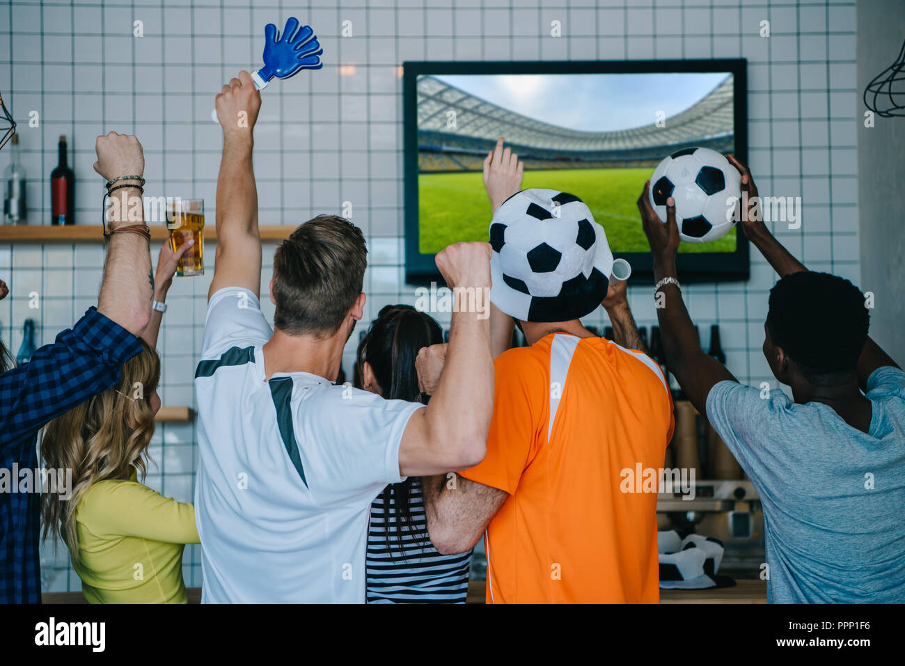 back view of football fans in soccer ball hats celebrating with hand ...