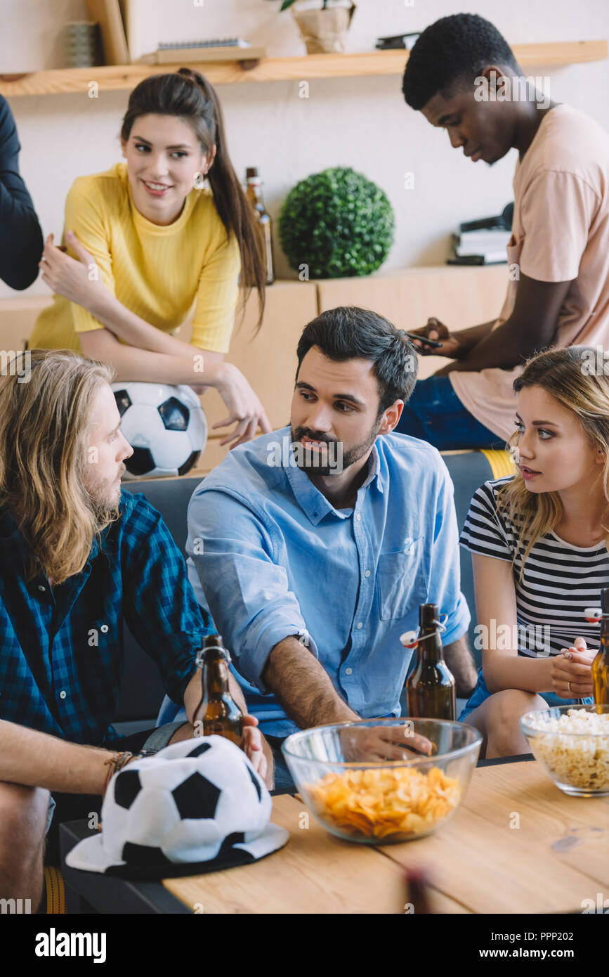 group multicultural football fans sitting on sofa and talking to each ...