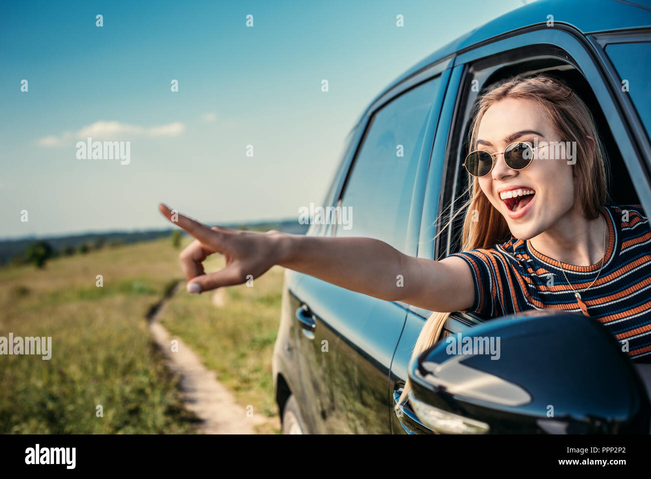 surprised young woman in sunglasses leaning out hand from car window ...
