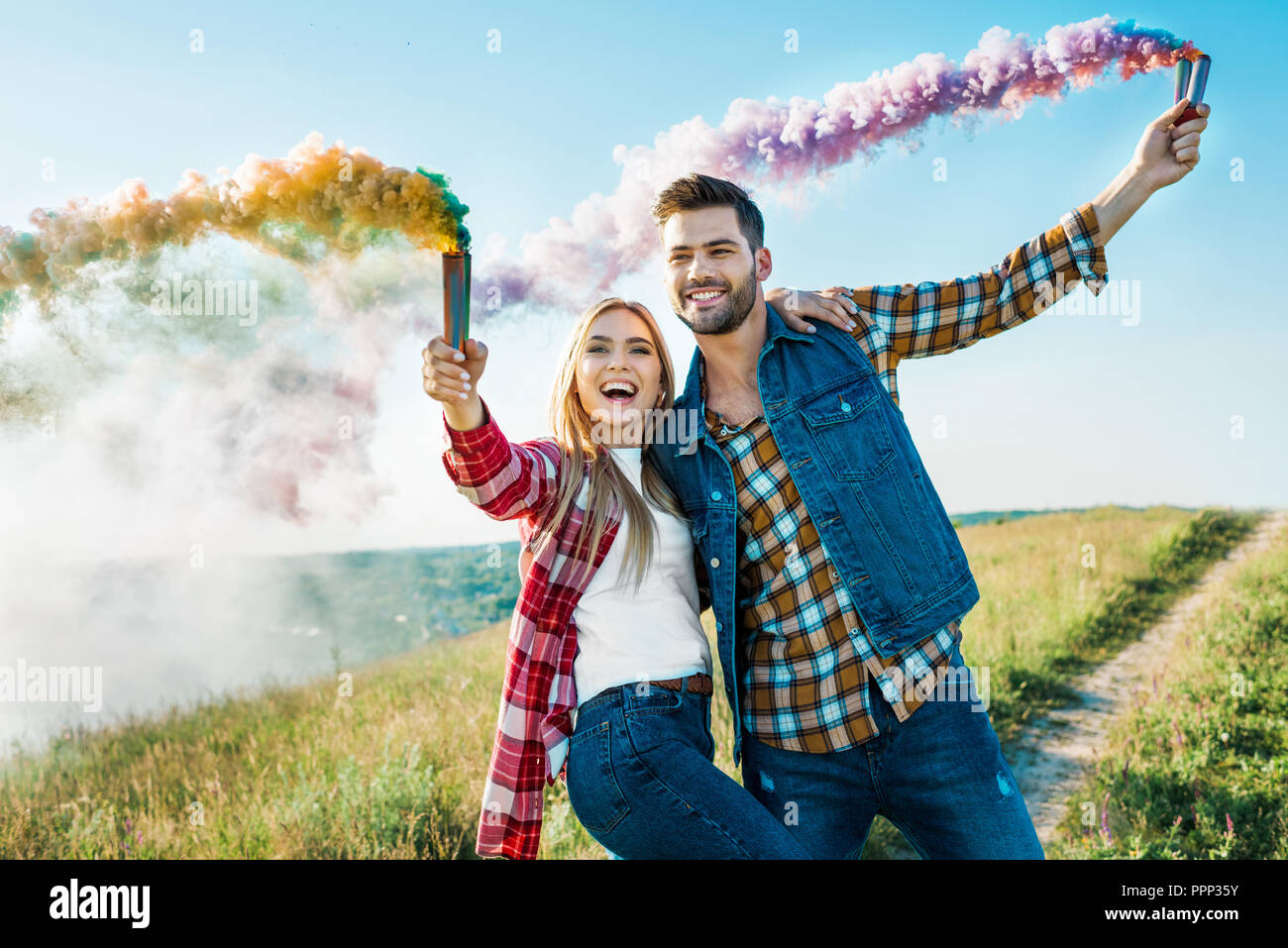 smiling couple holding colorful smoke bombs on rural meadow Stock Photo ...