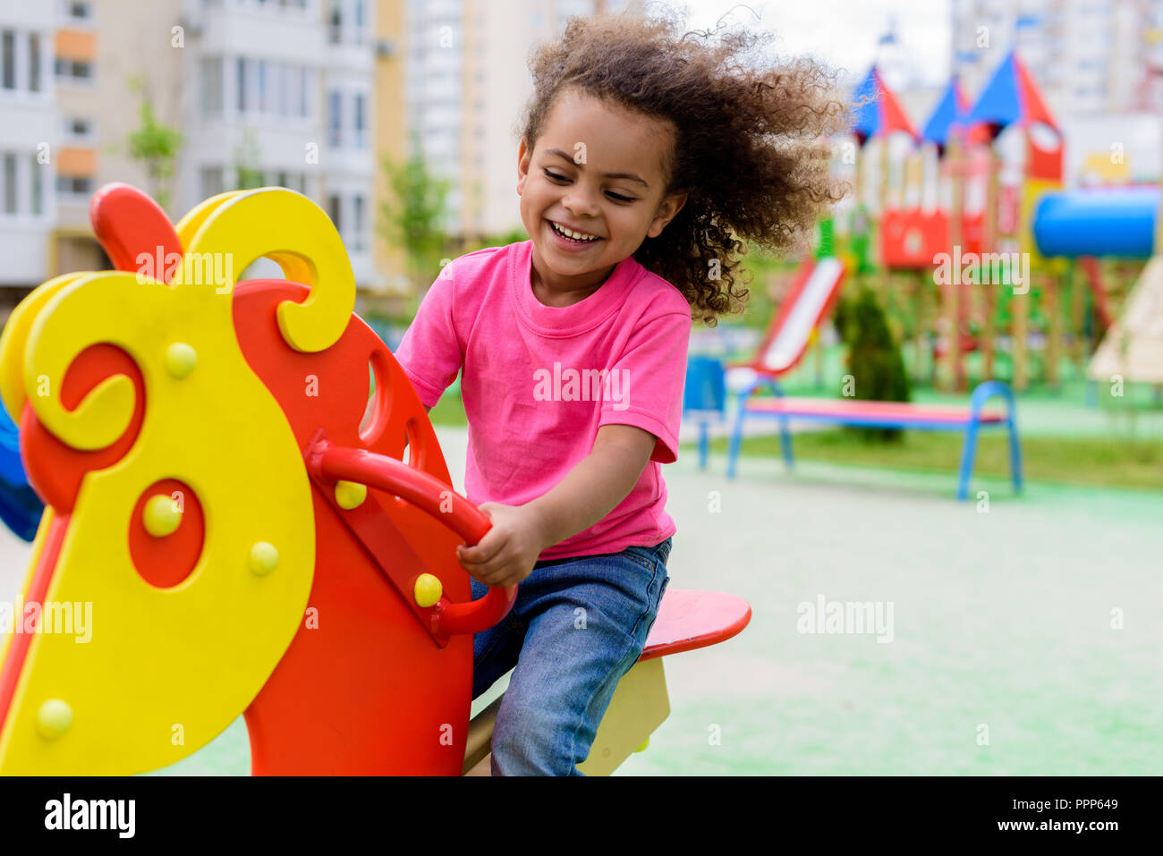 smiling curly african american little child riding on rocking horse at ...