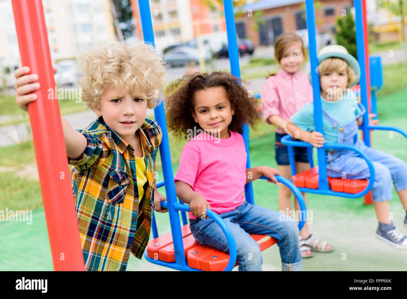 multicultural group of little children riding on swings at playground ...