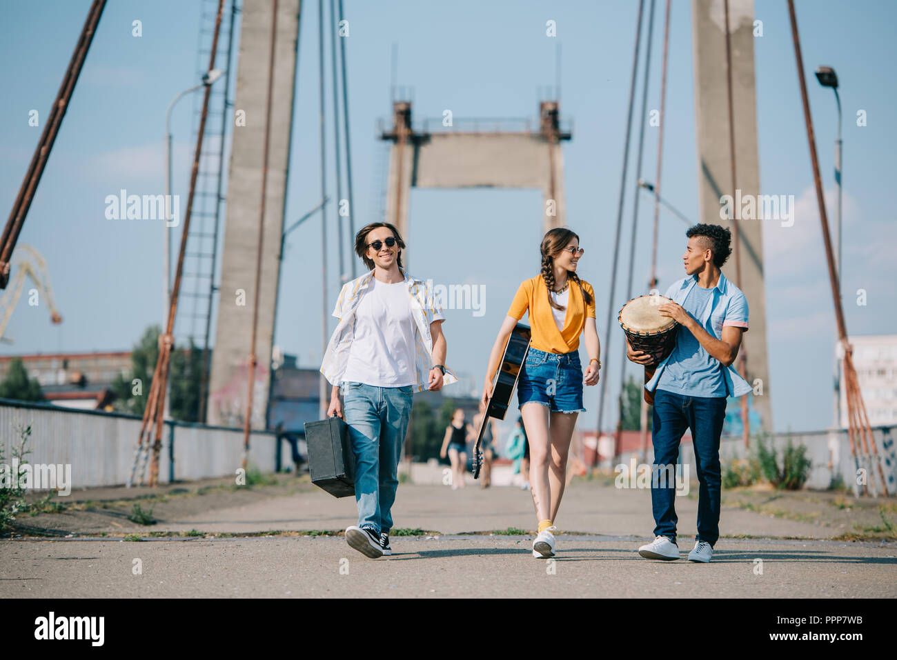 Young male and female buskers carrying instruments on sunny city street ...