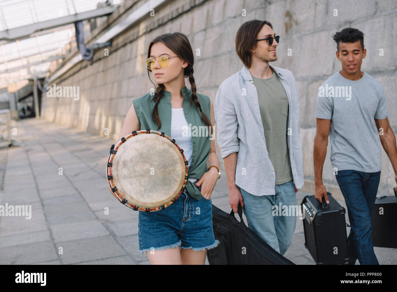 Team of young male and female friends walking and carrying musical ...