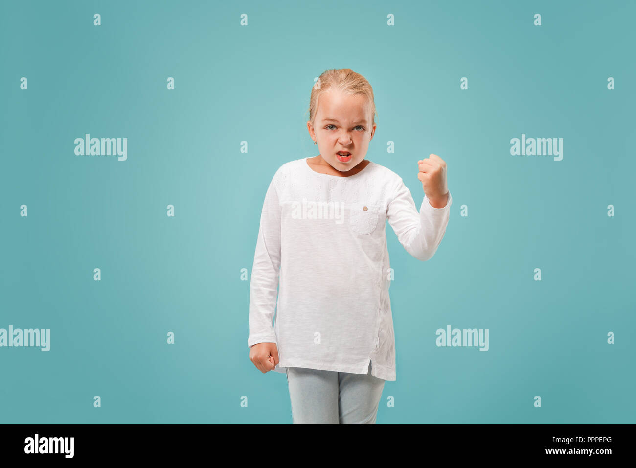 Angry teen girl standing on trendy blue studio background. Female half ...