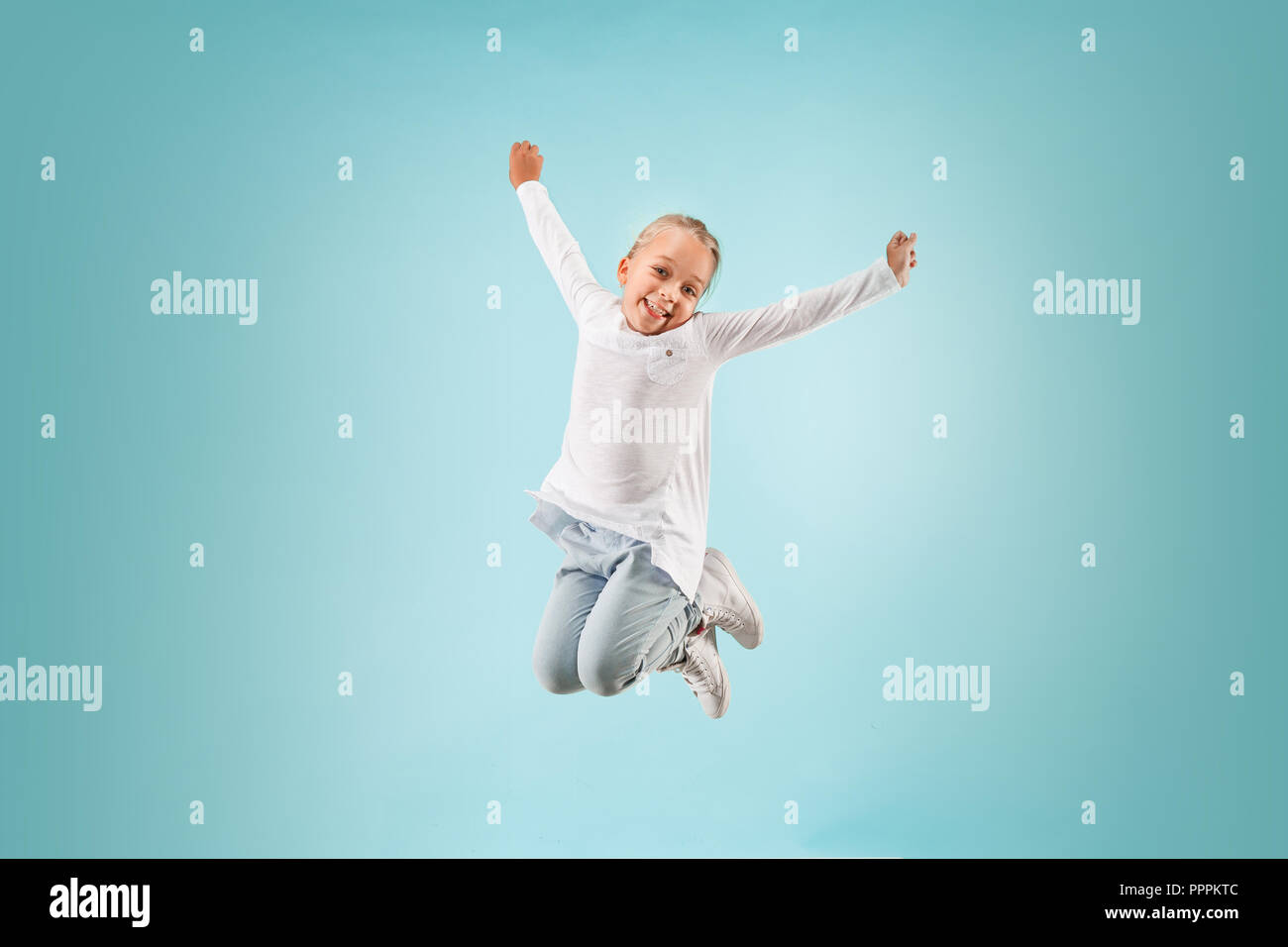Adorable small child at blue studio. The girl is jumping and smiling ...