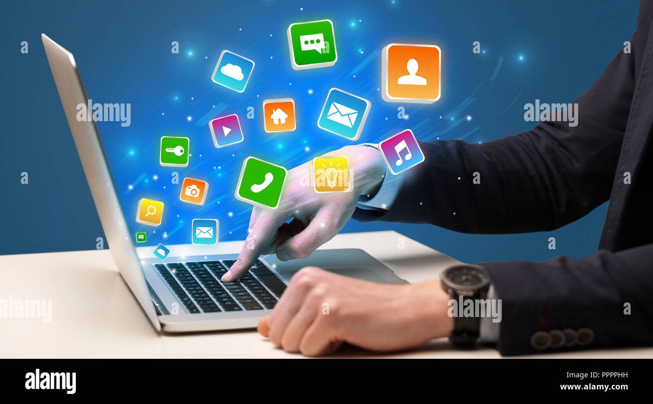 Businessman hand typing on laptop with flying application icons around ...