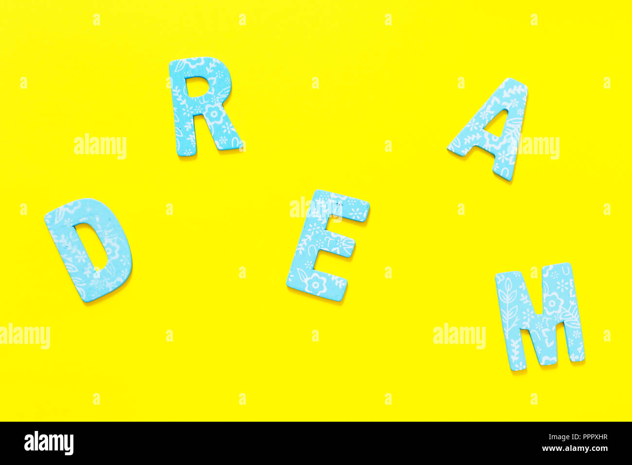 Word DREAM made out of small blue wooden letter on yellow background ...