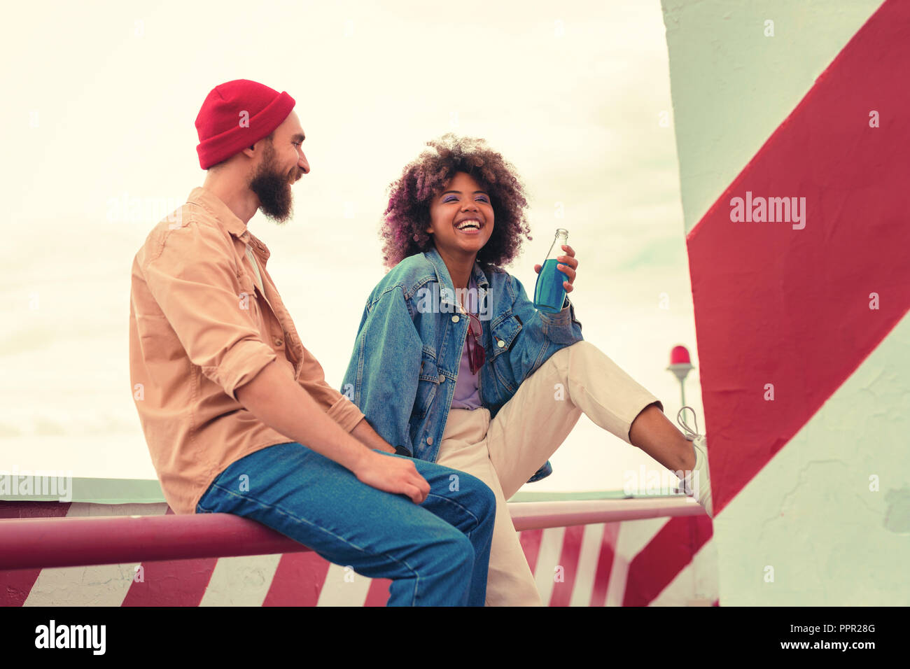 Cheerful couple smiling while sitting on the roof and drinking blue ...