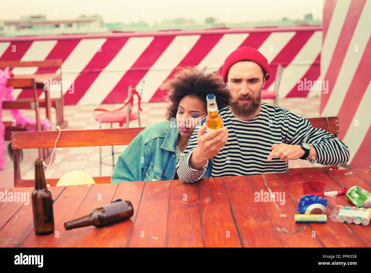 Frowning man looking at the bottle of beer while his girlfriend ...