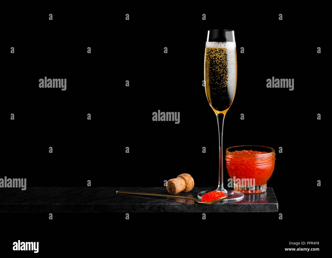 Elegant glass of yellow champagne with red caviar on golden spoon and ...
