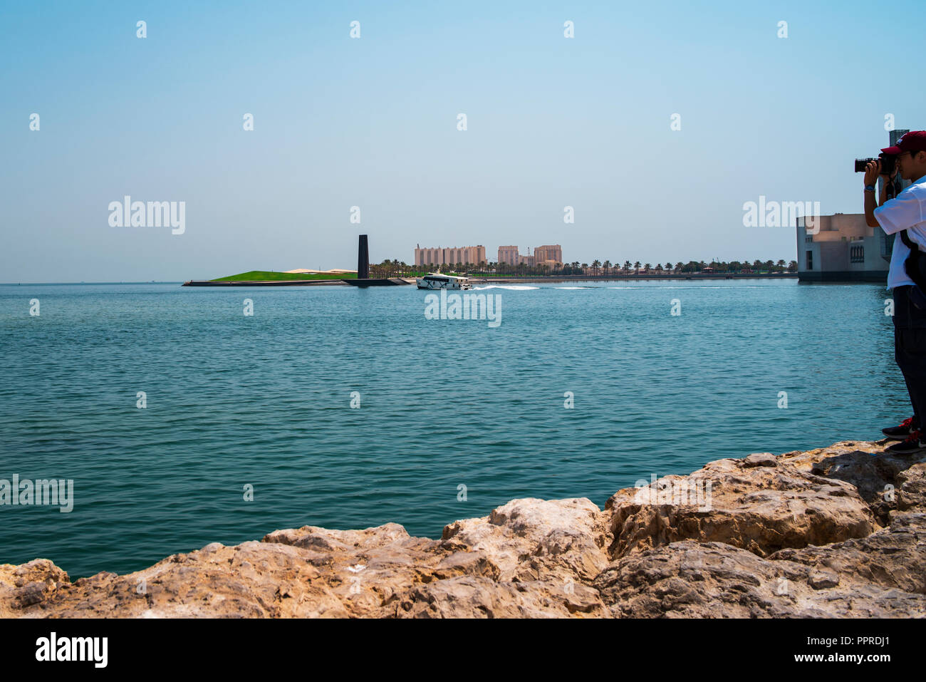 A man with a camera stands on Corniche Broadway and Looking on the Doha ...