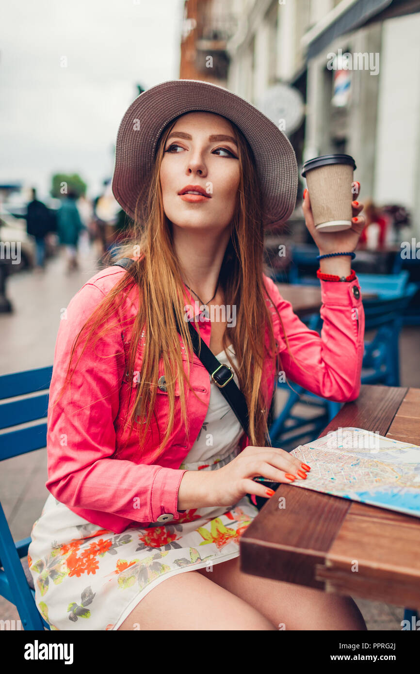 Young tourist woman having coffee in outdoor cafe while checking map ...