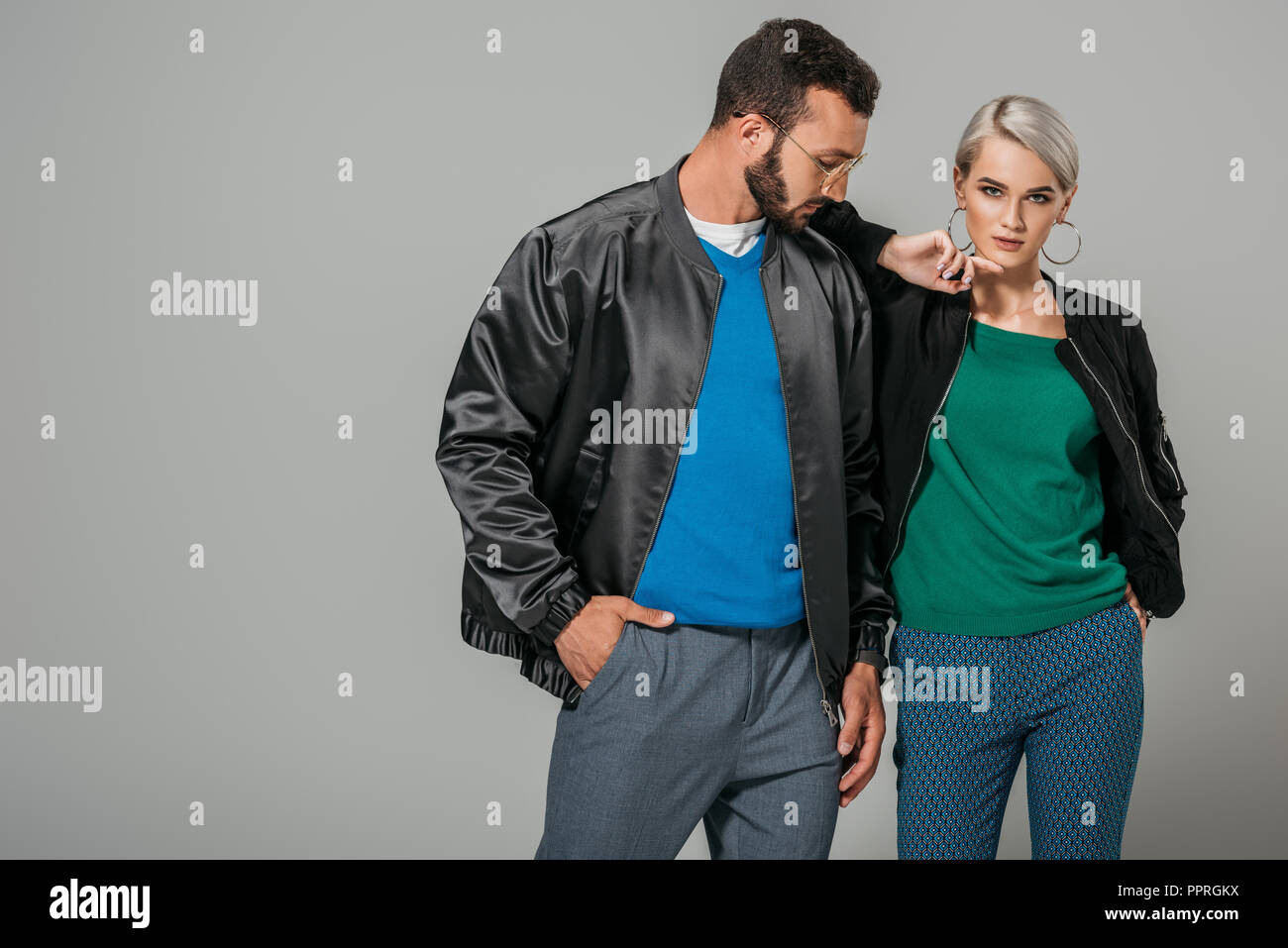 serious couple of models in stylish outfits isolated on grey background ...