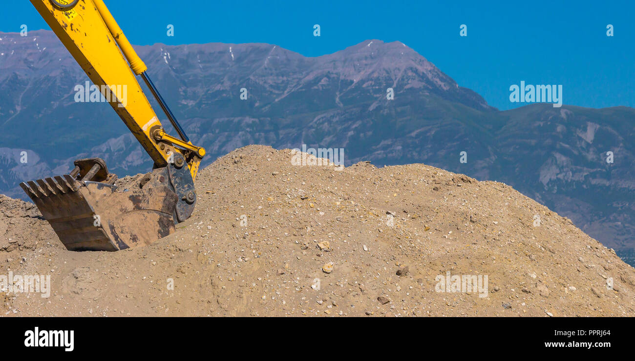 Excavator arm scooping dirt in front of mountain Stock Photo - Alamy
