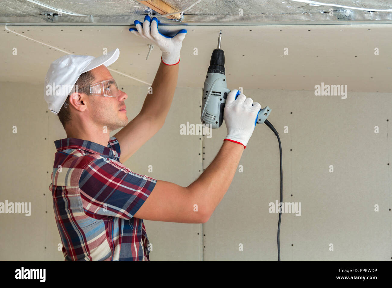 Young man in goggles fixing drywall suspended ceiling to metal frame ...