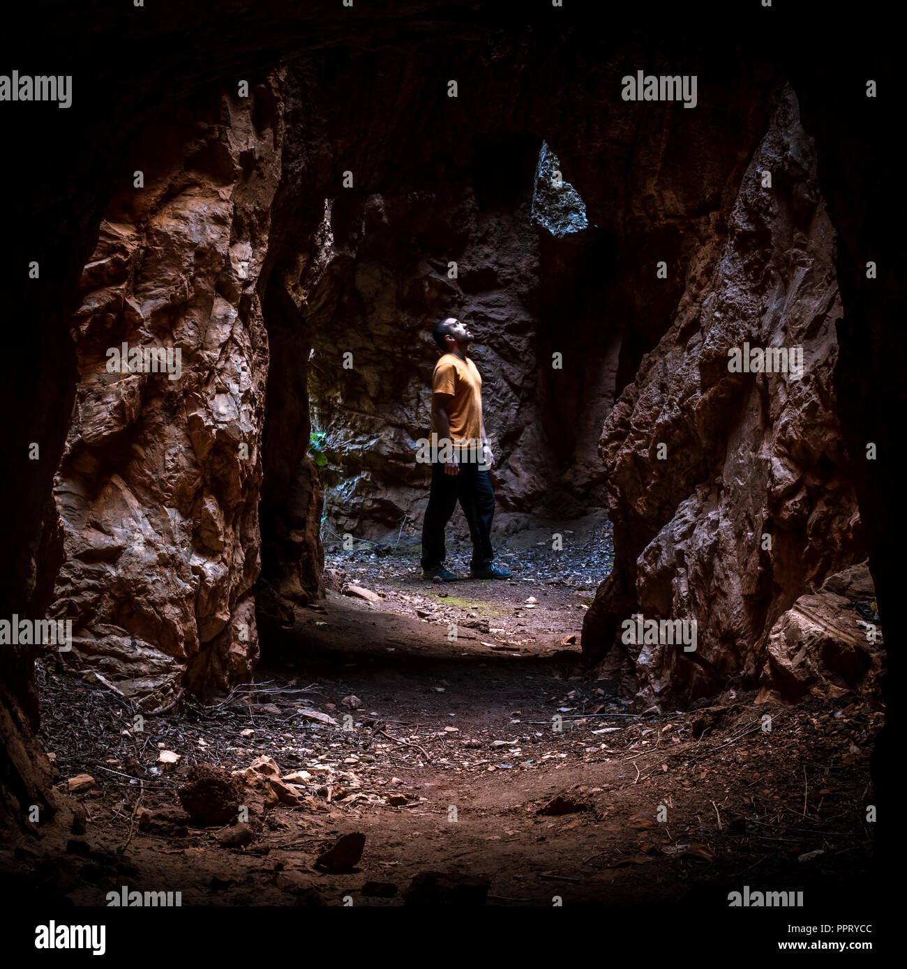 Side view of adult tourist man standing and looking up on cave entrance ...