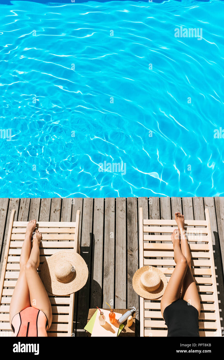 cropped shot of young women in swimwear resting on chaise lounges near ...