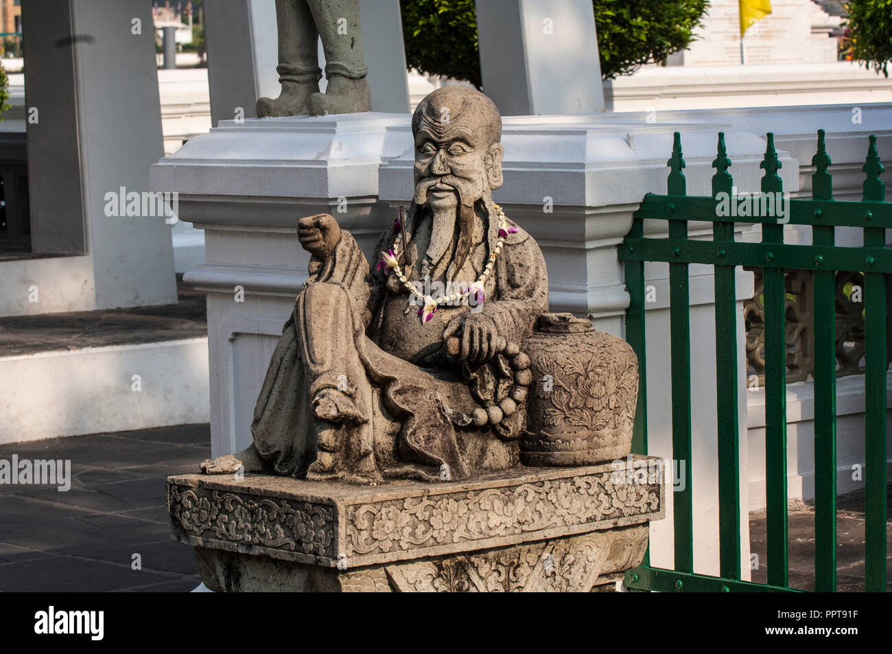 Stone guardian statue in seated position with a garland of orchids, Wat ...