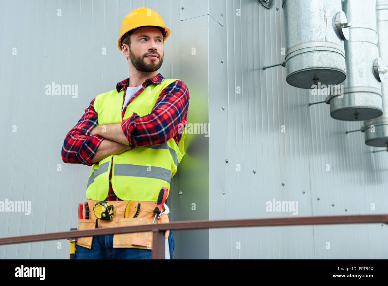 male professional engineer with tool belt posing with crossed arms at ...