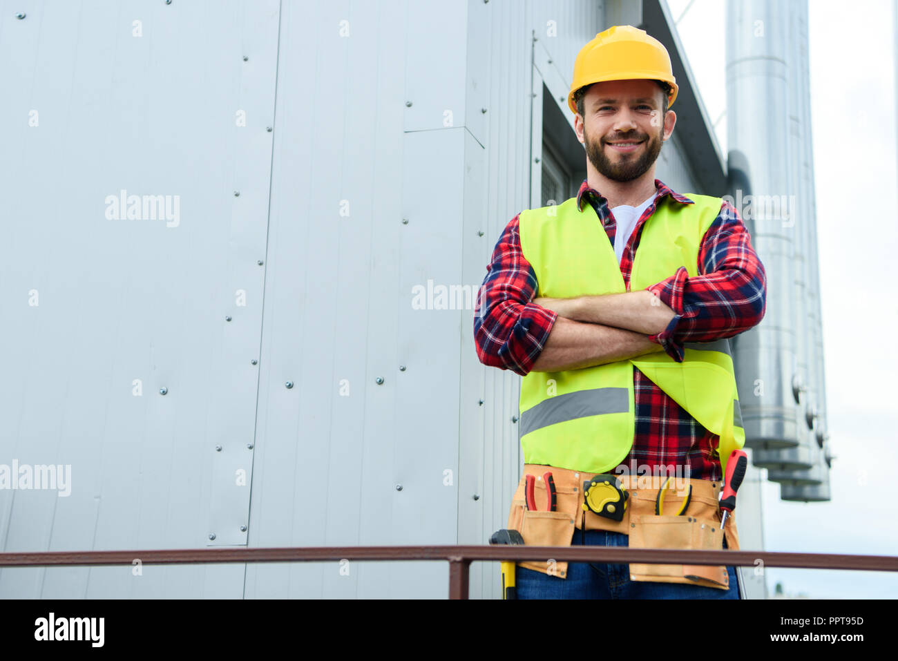 male professional engineer with tool belt posing with crossed arms ...