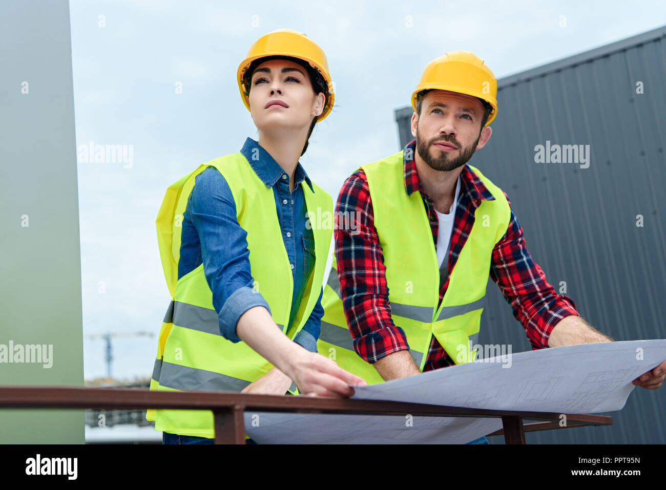 professional engineers in helmets working with blueprints and looking ...