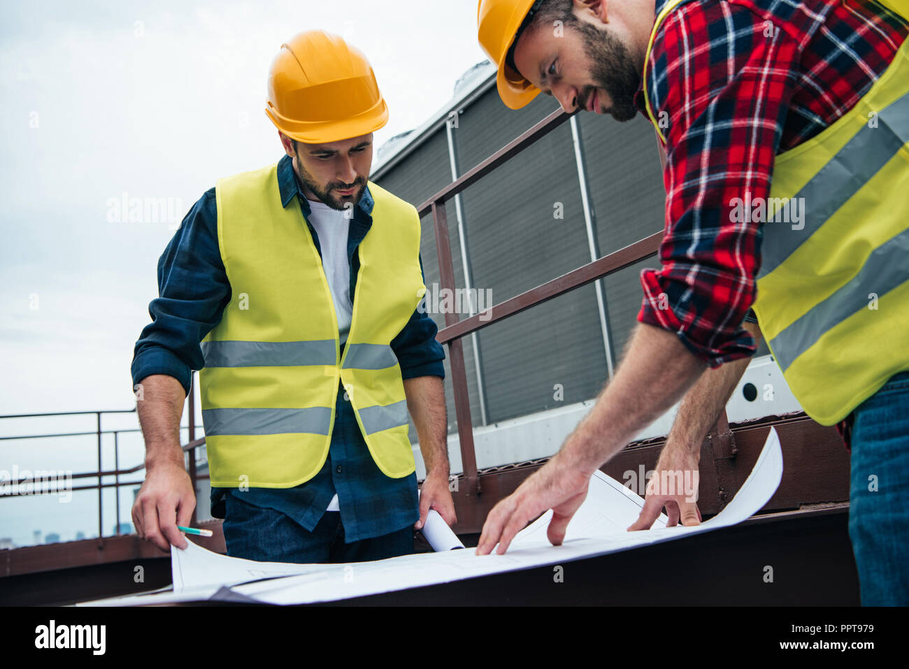 architects in safety vests and hardhats working with blueprints on roof ...