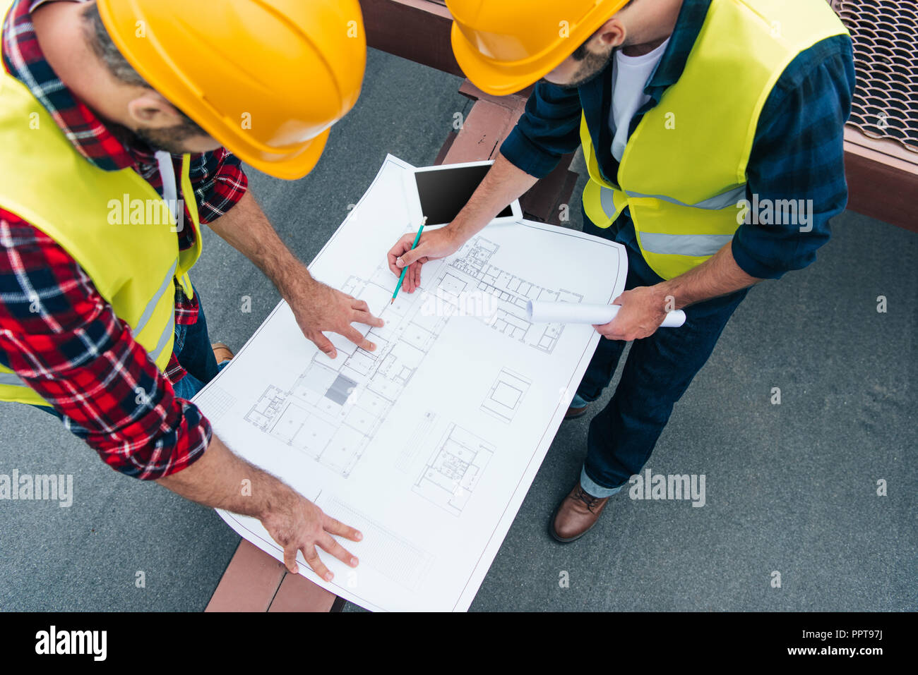 overhead view of architects in safety vests and helmets drawing on ...