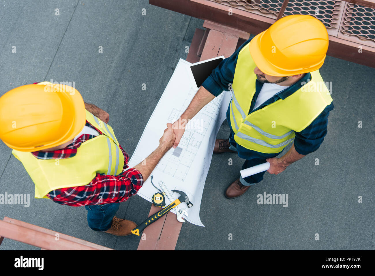 overhead view of engineers in helmets with blueprints shaking hands on ...