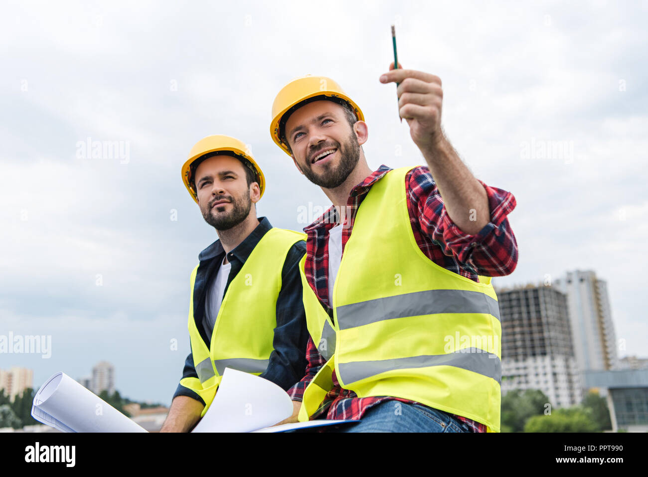 two architects in safety vests and hardhats working with blueprints and ...