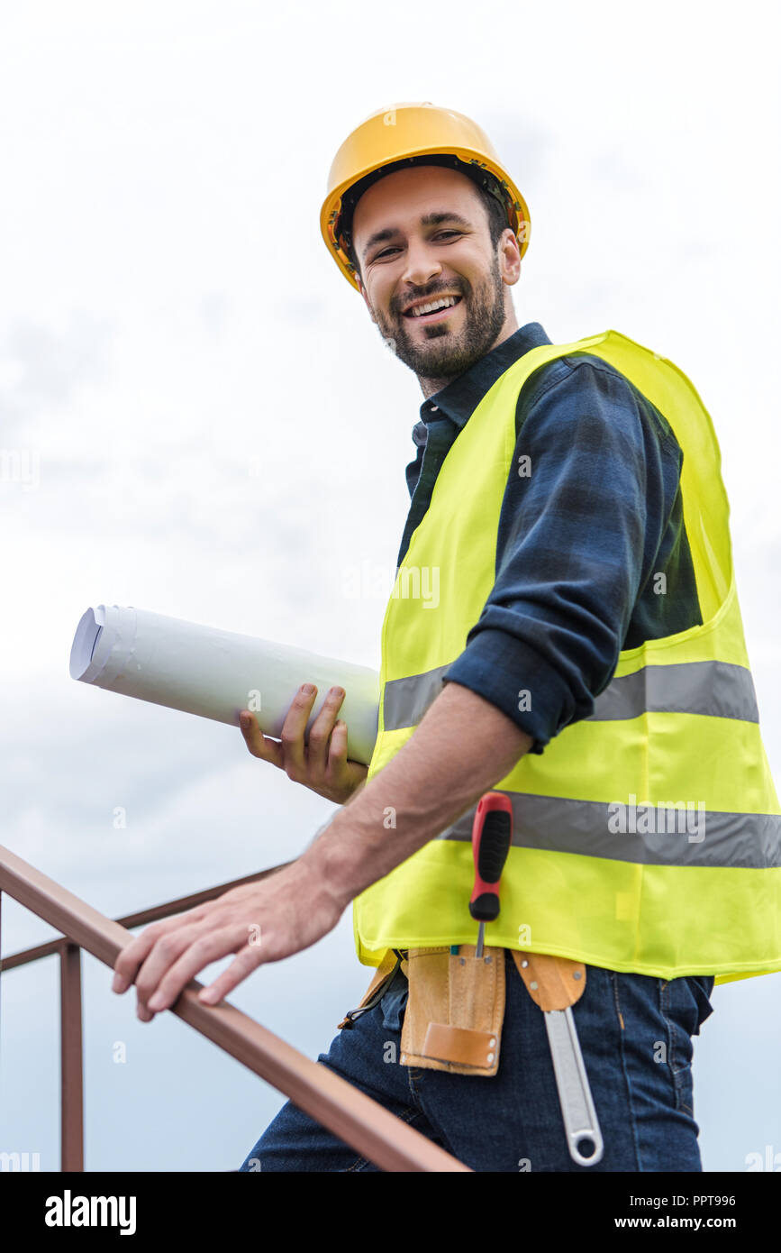 smiling engineer in safety vest with tool belt and blueprint Stock ...