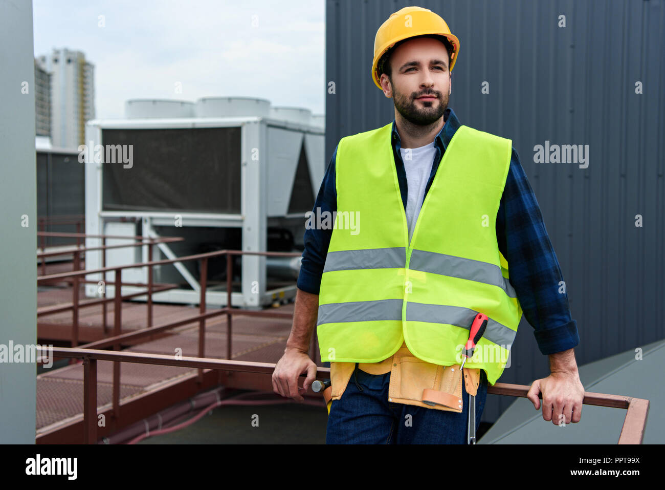 male architect in safety vest and hardhat with tool belt standing on ...