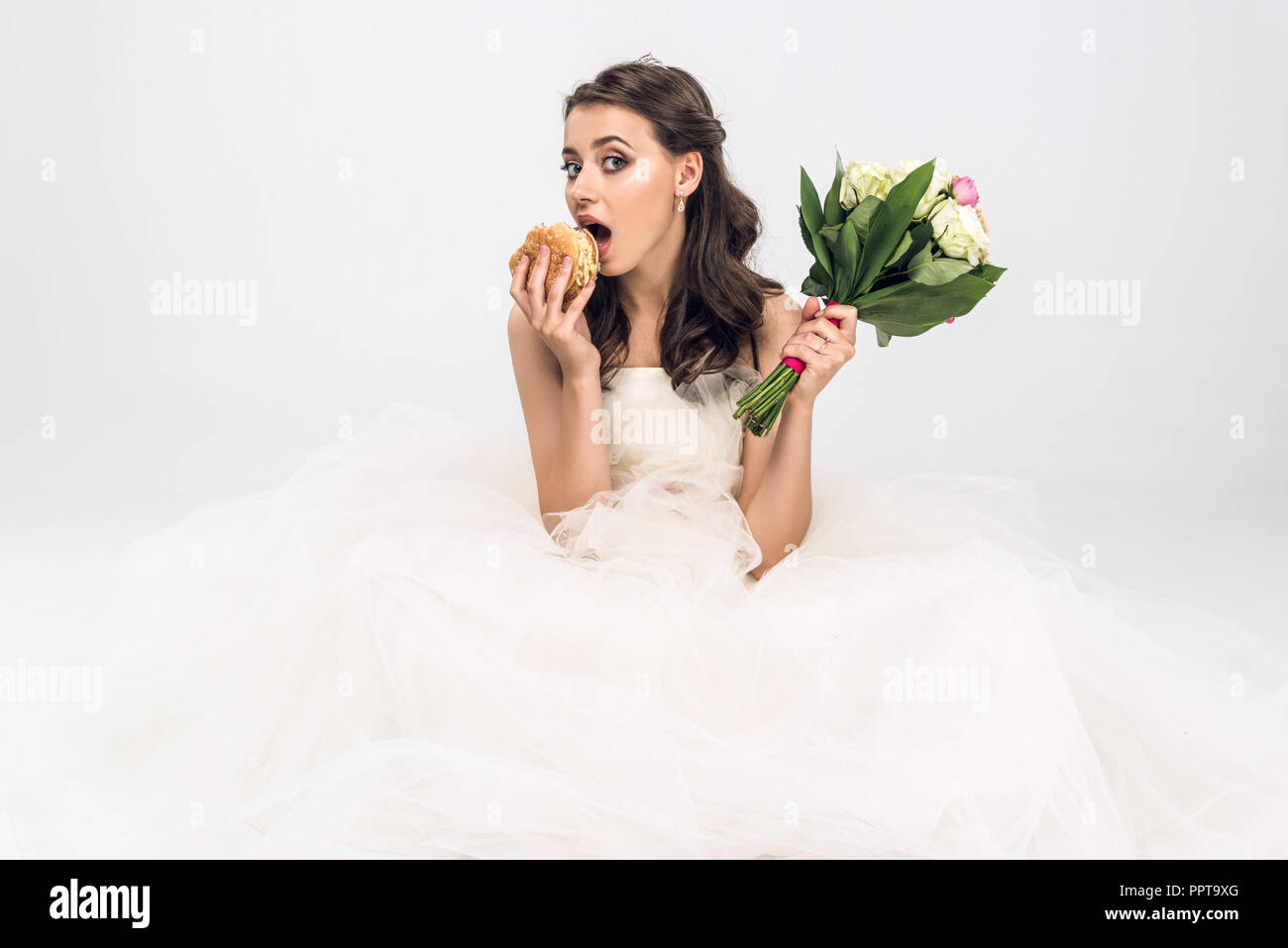 shocked young bride in wedding dress sitting on floor with burger and ...