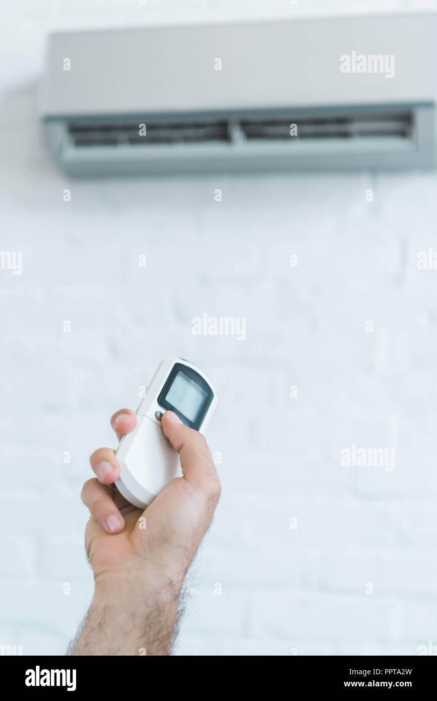 cropped view of man turning on air conditioner with remote control ...