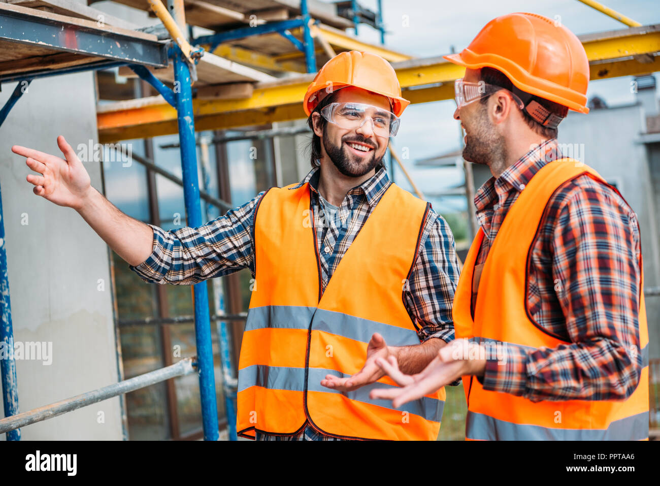 happy builders in reflective vest and hard hat pointing at building ...