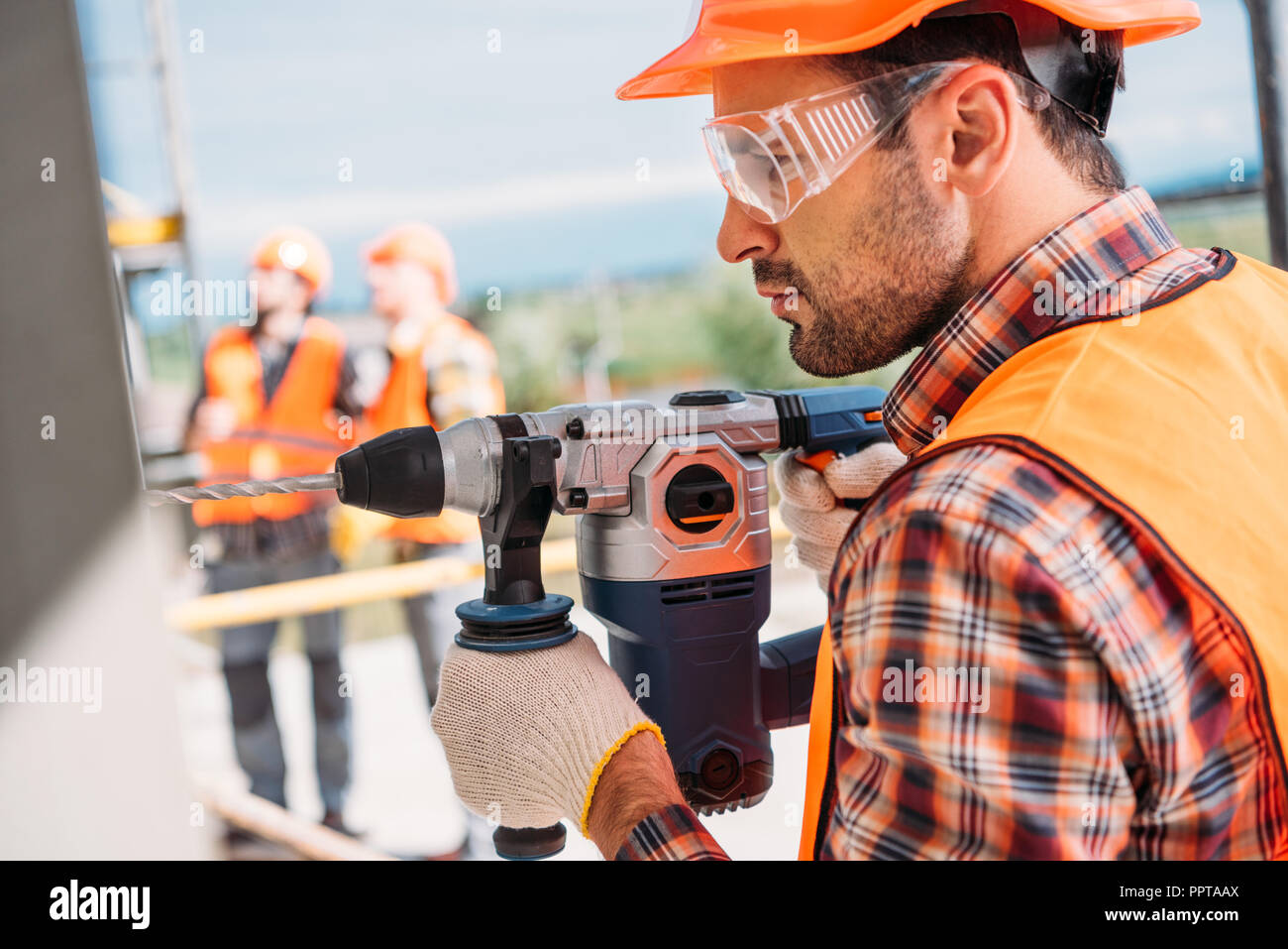 side view of builder in protective helmet and eyeglasses using power ...