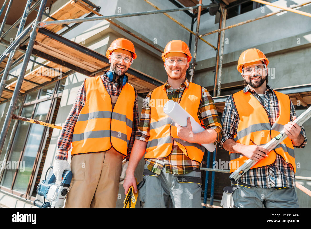 bottom view of group of happy equipped builders looking at camera at ...