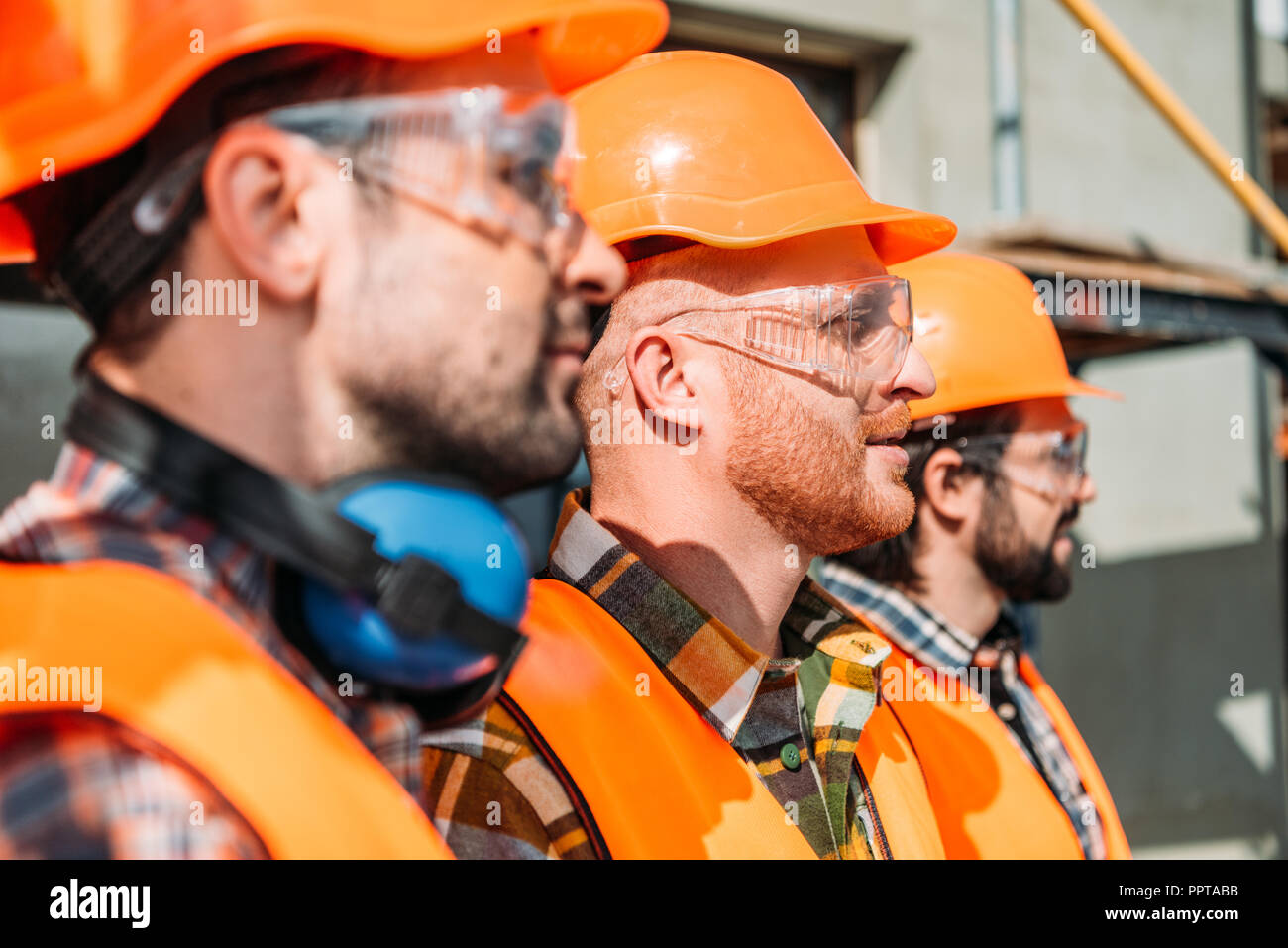 side view of group of equipped builders standing at construction site ...
