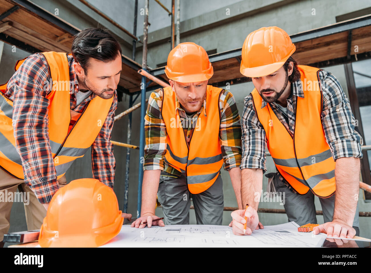 group of confident builders looking at building plan at construction ...