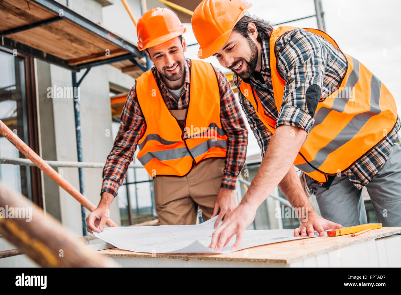 handsome smiling builders looking at construction plan Stock Photo - Alamy