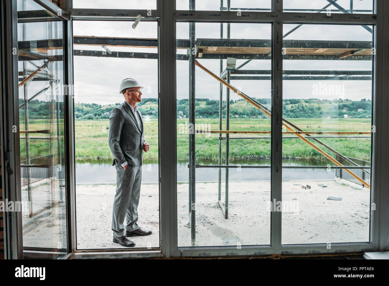 handsome architect in suit and hard hat standing on terrace at ...