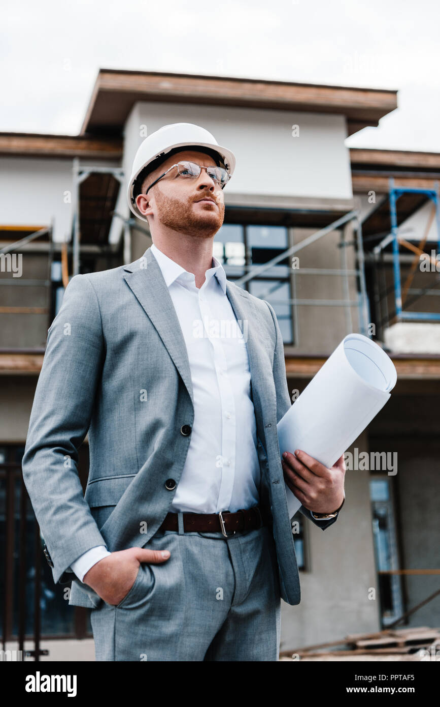 handsome architect in suit and hard hat holding blueprint standing in ...