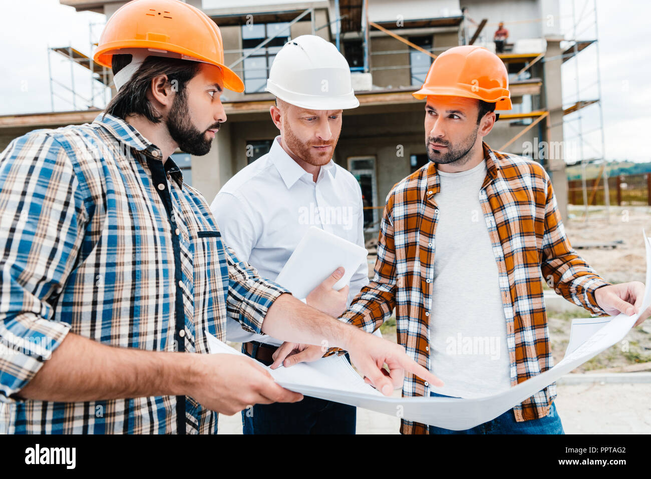 group of architects with building plan having conversation in front of ...
