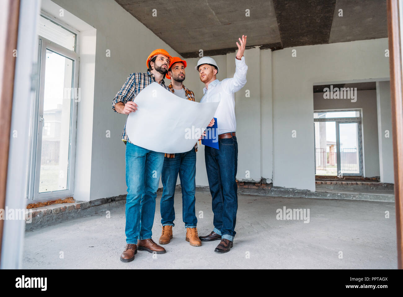 group of architects with blueprint having conversation and looking away ...
