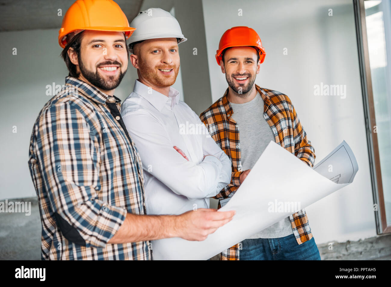 group of architects with blueprint inside of constructing building looking at camera Stock Photo ...