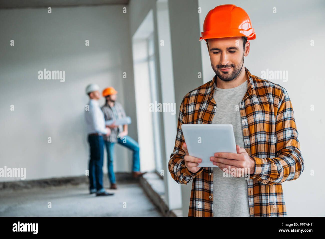 handsome architect in plaid shirt and hard hat standing inside of ...