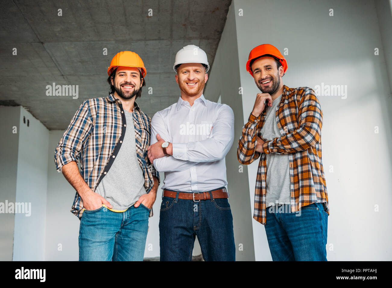 group of smiling architects inside of constructing building looking at ...